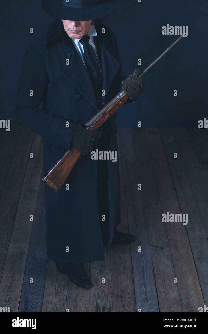Victorian man in long black coat and hat holding rifle Stock Photo - Alamy