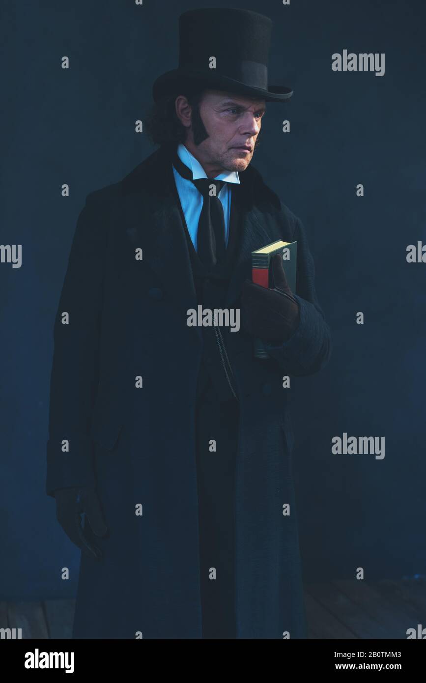 Edwardian man in long black coat and hat holding book Stock Photo - Alamy