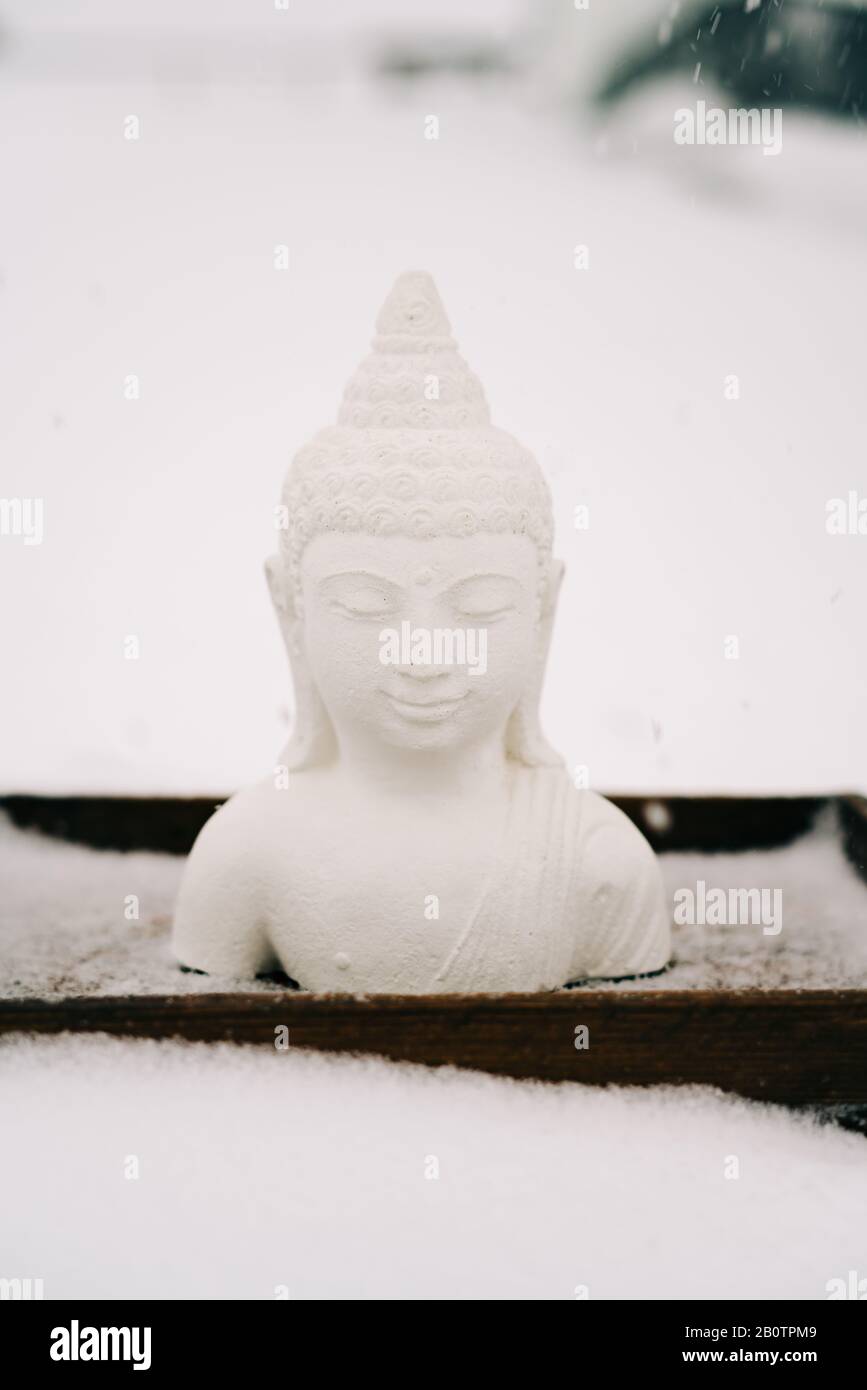 white Buddha figurine made of plaster on a wooden stand during a ...