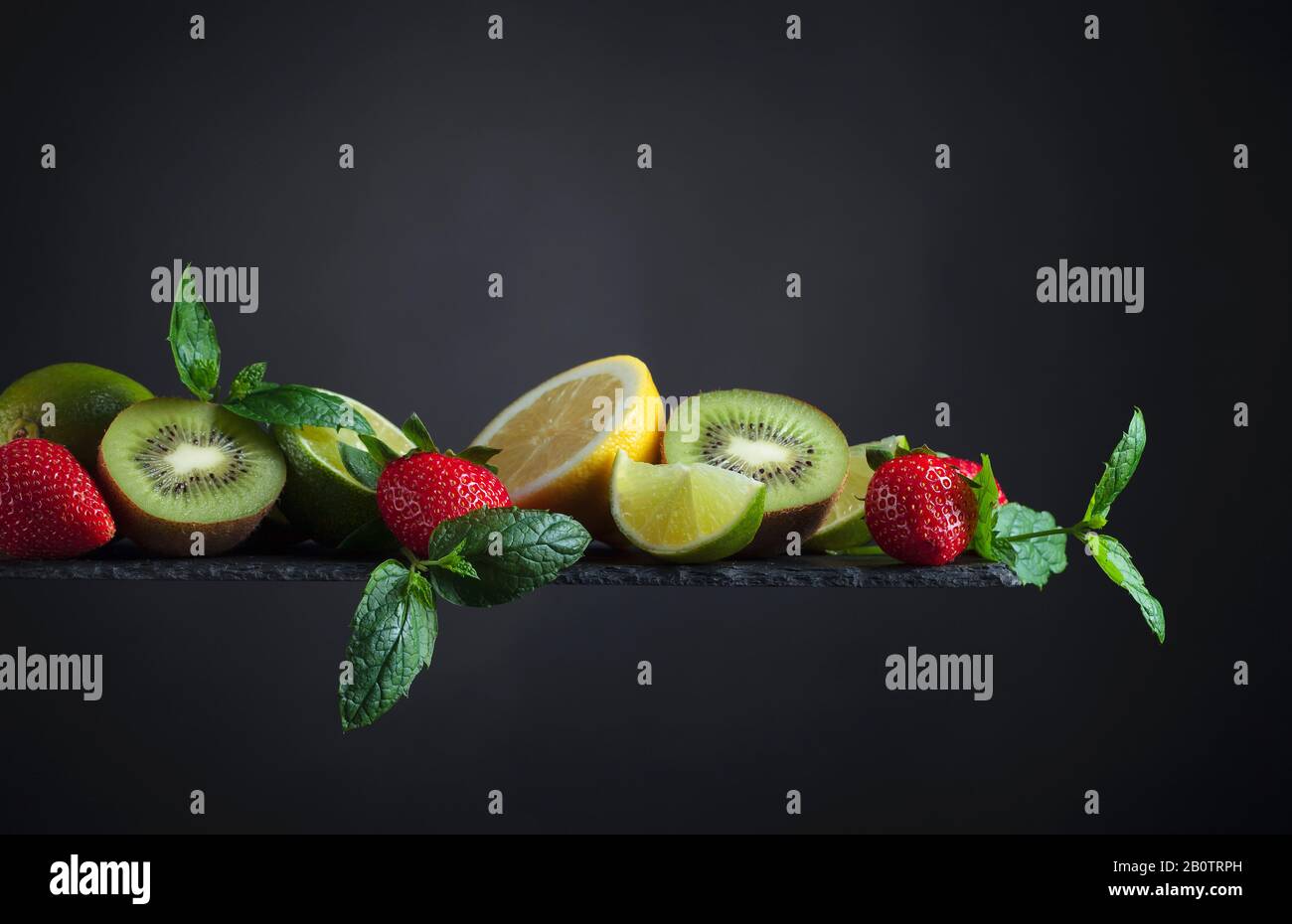 Fresh fruits and berries with mint on a black background. Copy space ...