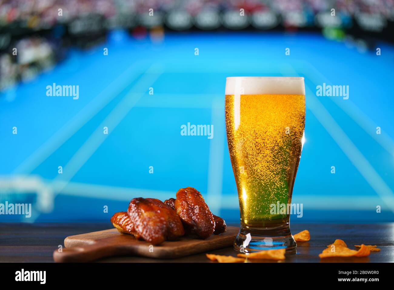 Spicy barbecue chicken wings, nachos and beer on dark wooden bar table ...