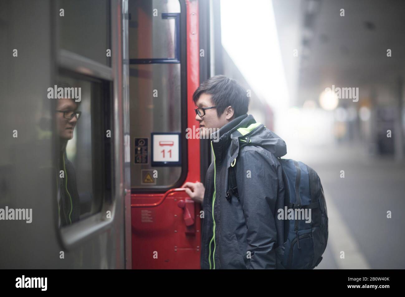 Young Asian man wearing glasses on railway platform, entering passenger ...