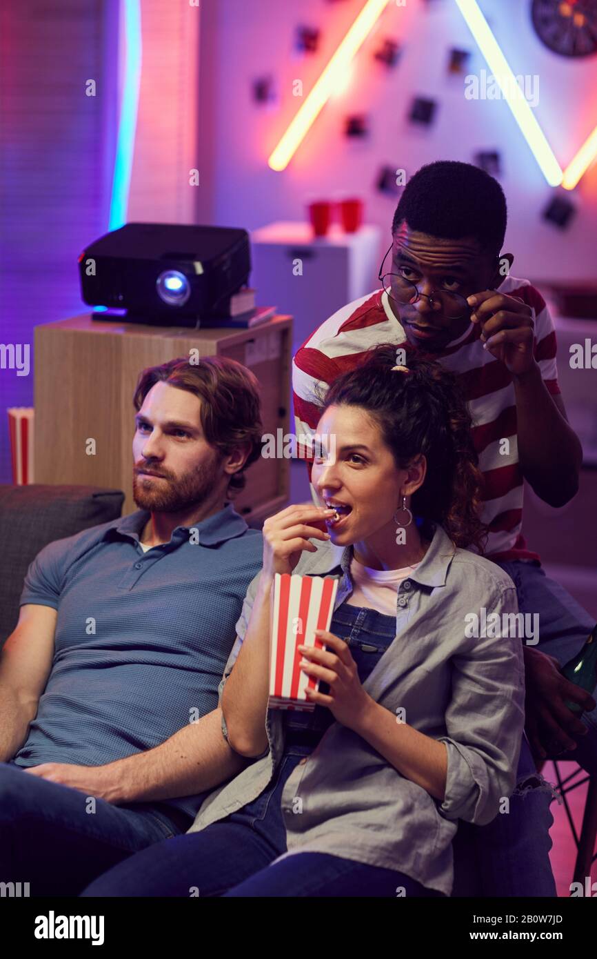 Young friends sitting together eating popcorn and watching a movie ...