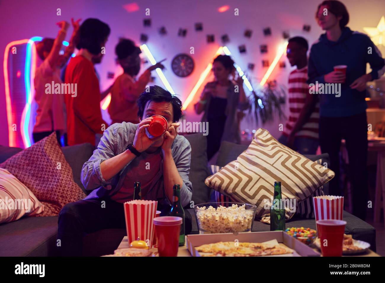 Young man sitting on sofa and drinking alcohol while his friends ...
