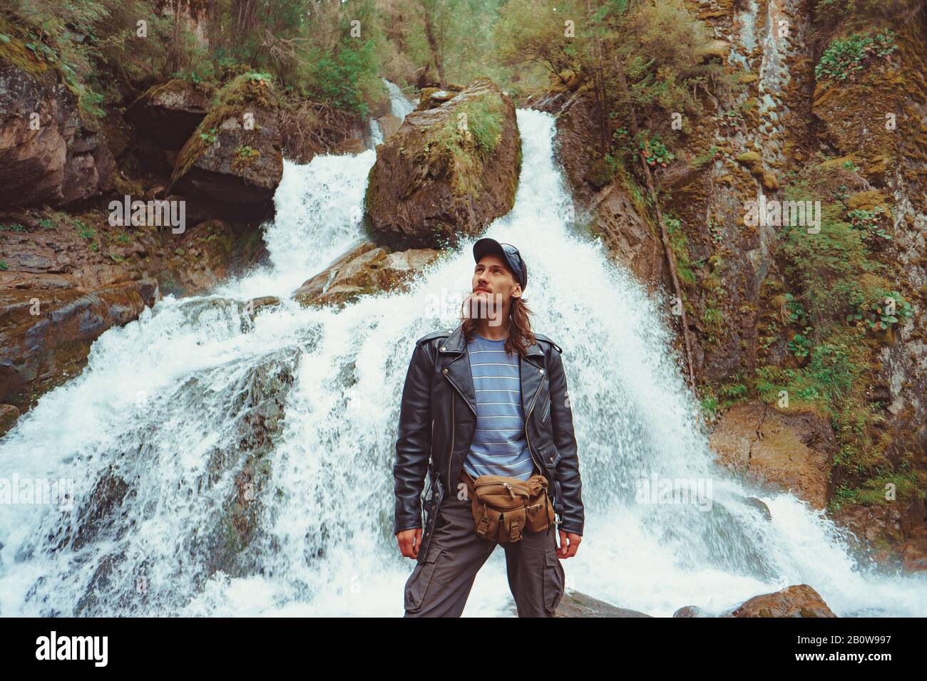 a guy in a leather jacket with long hair stands at a waterfall Stock ...