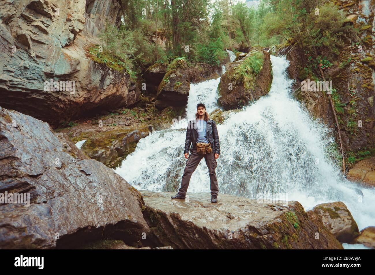 a guy in a leather jacket with long hair stands at a waterfall Stock ...
