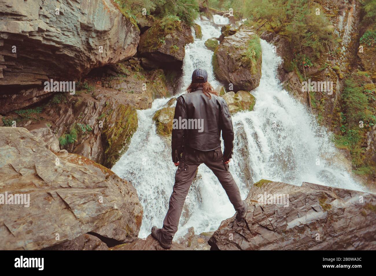 a guy in a leather jacket with long hair stands at a waterfall Stock ...