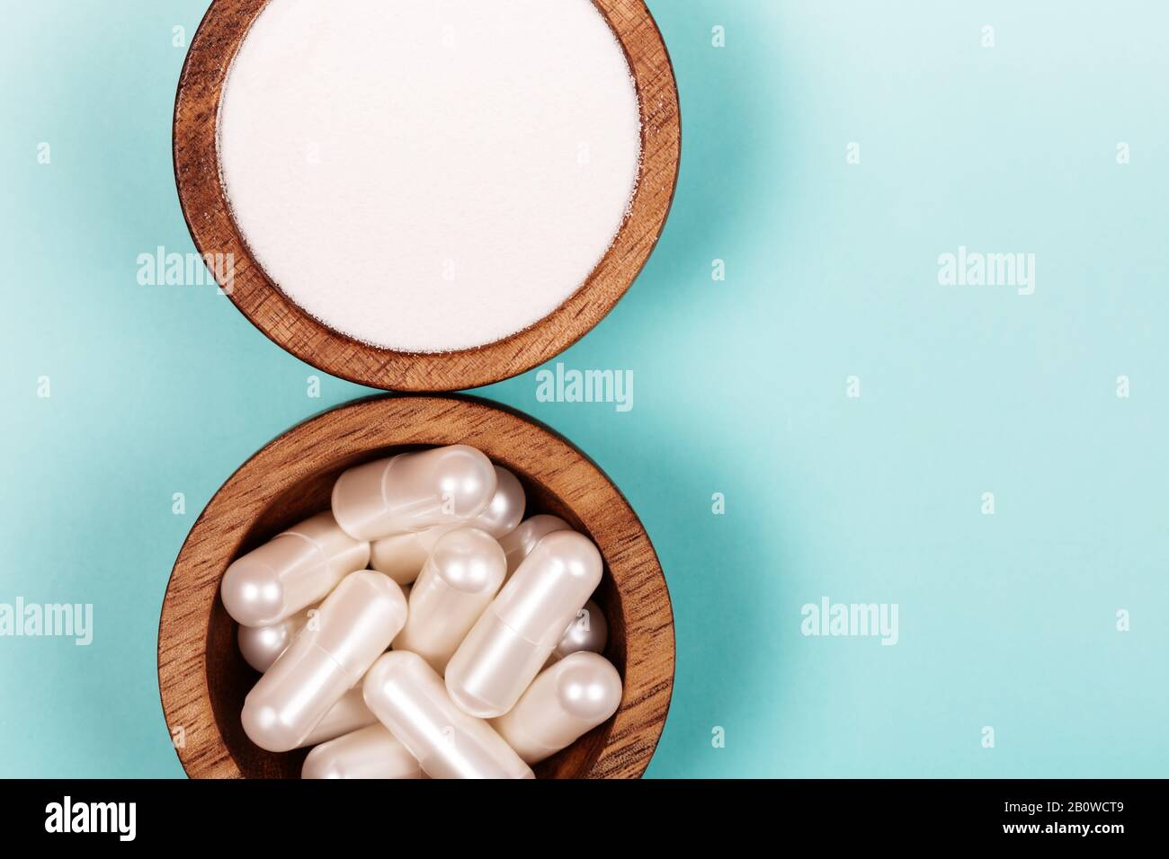 Collagen in capsules and in powder in two wooden bowls on pastel blue ...