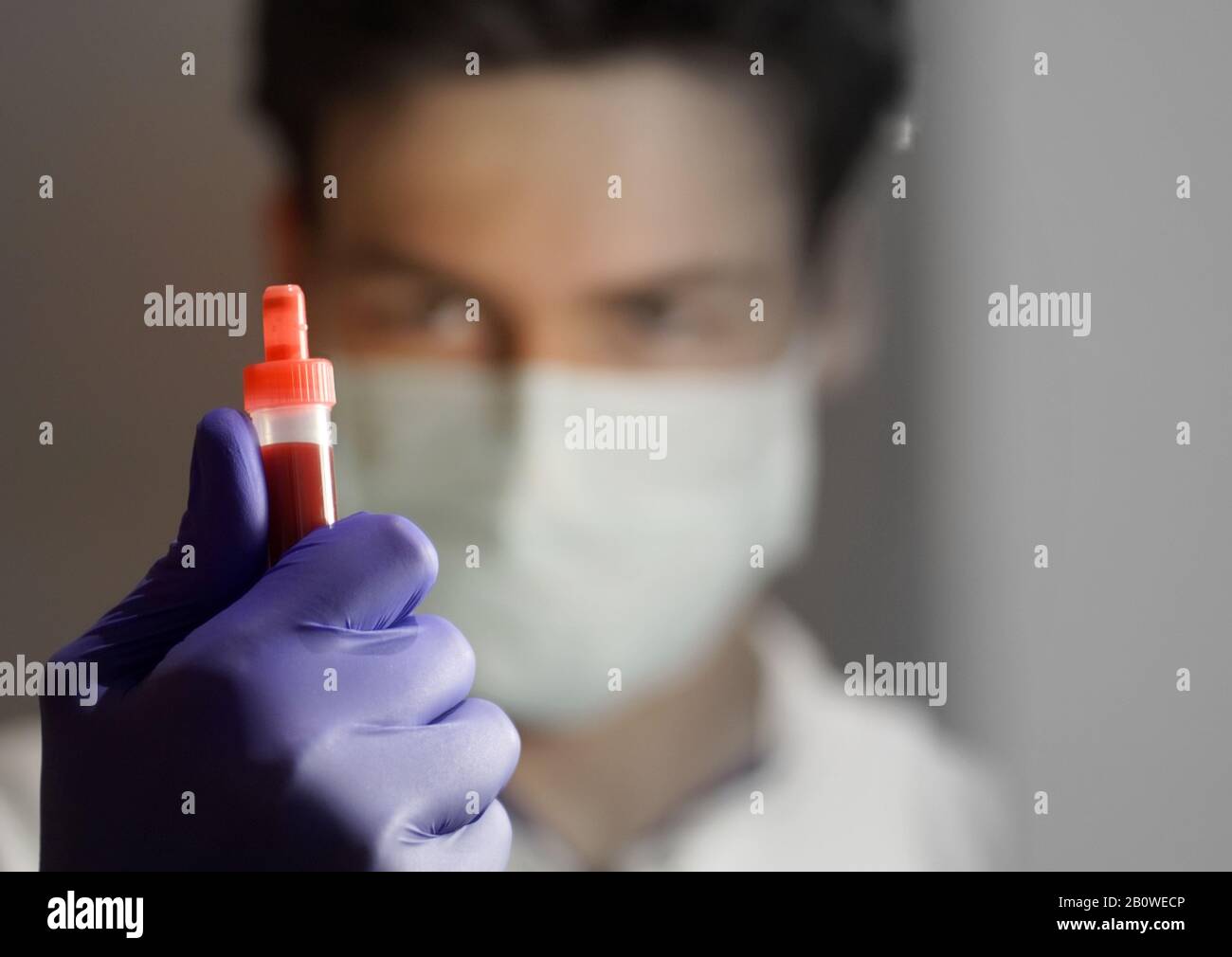Close of of a blood sample held by medical lab staff in the background ...