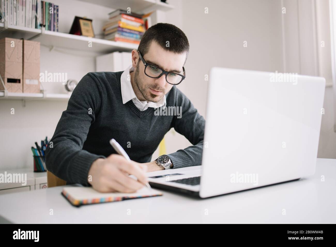 Office employee sitting on desk and writing in notebook. Businessman ...