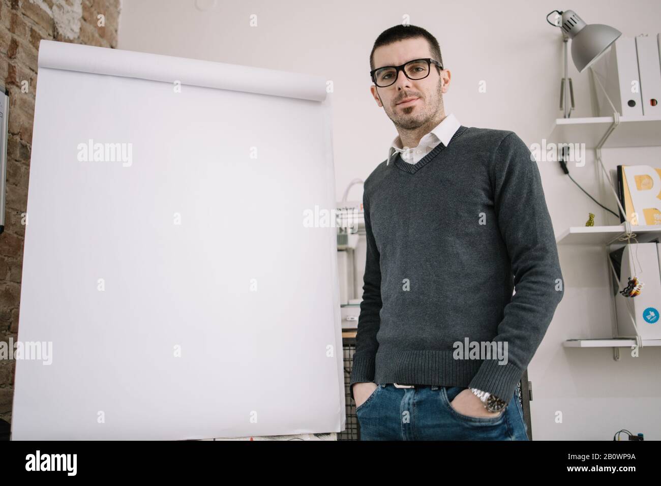 Young businessman standing near flip chart with hands in pockets ... Young businessman standing near flip chart with hands in pockets ...