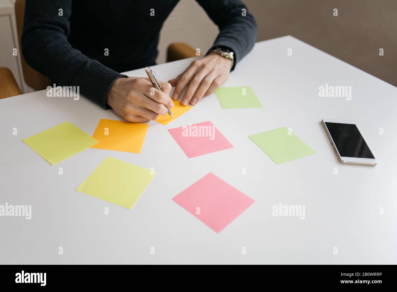 Hand holding pen writing on blank colorful sticky note. Cropped man ...