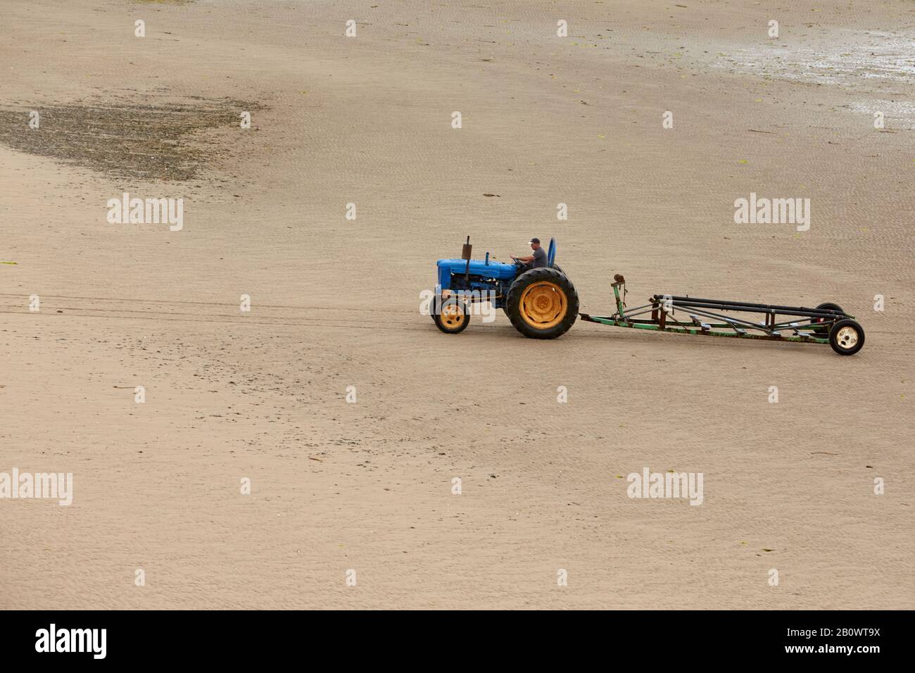Blue boat recovery tractor towing empty trailer along the beach in ...