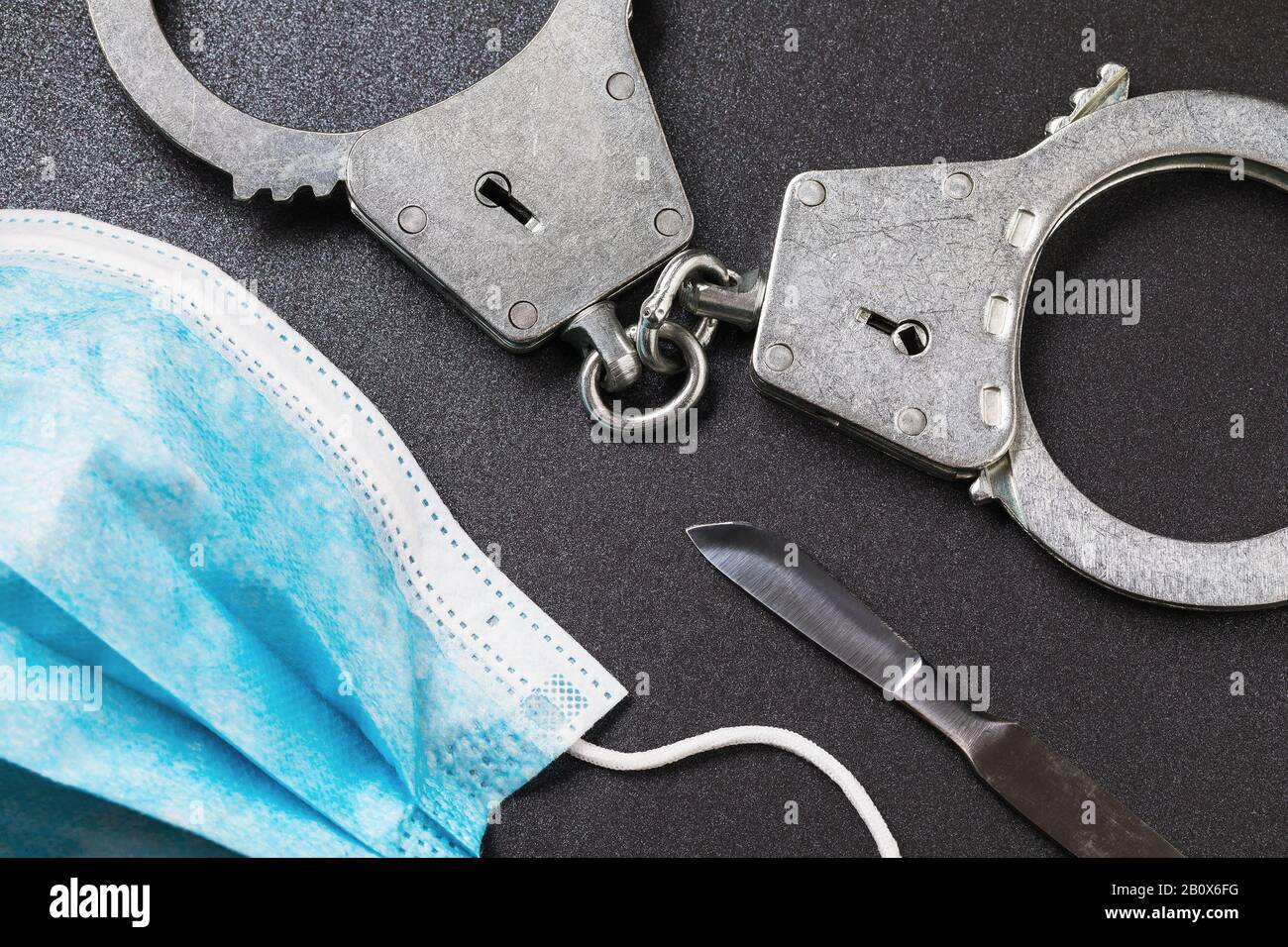 Handcuffs, scalpel and medical mask on the table. view from above ...