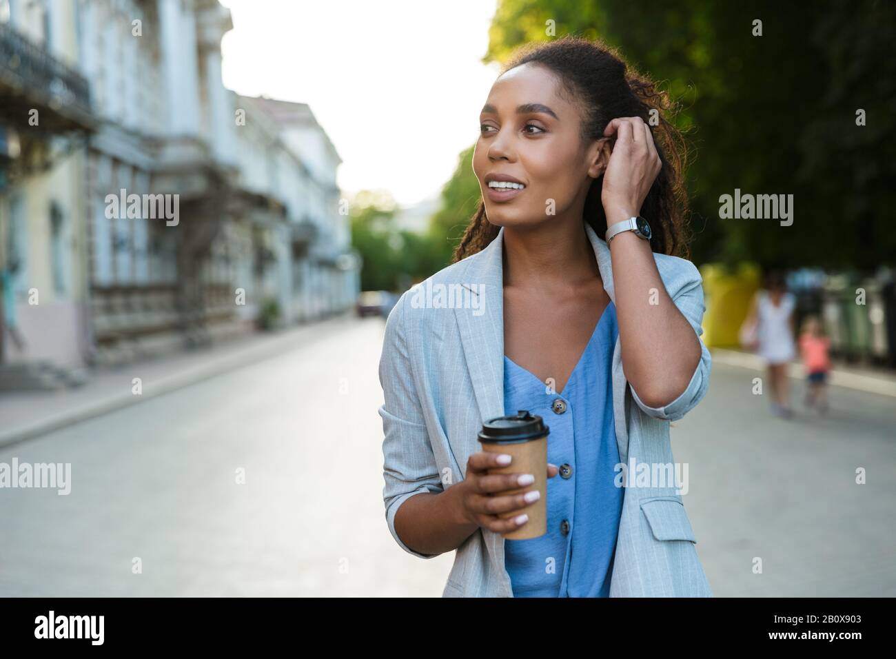 Attractive smiling african business woman standing outdoors at the city ...