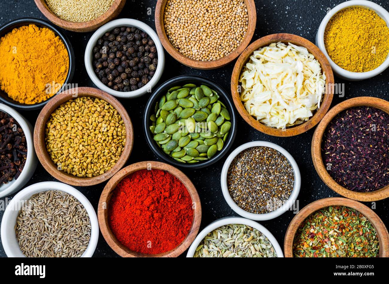 Variety of colorful spices, herbs, and seeds on black stone background ...