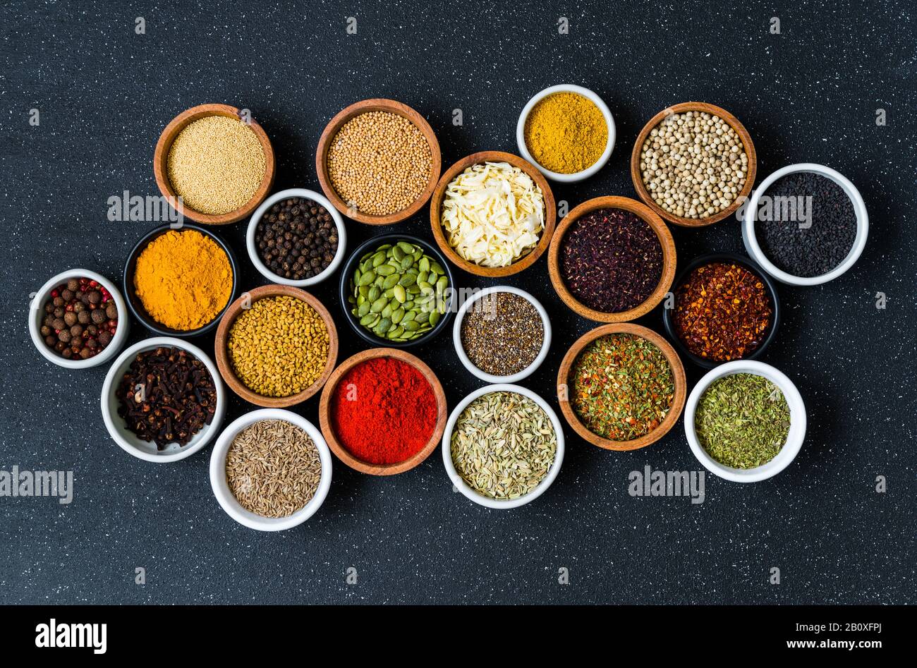 Variety of colorful spices, herbs, and seeds on black stone background ...