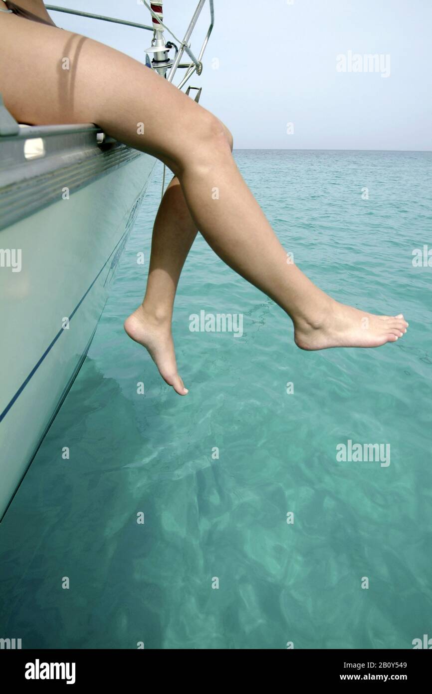 Young woman with dangling legs on a sailing yacht, Cala Ratjada ...