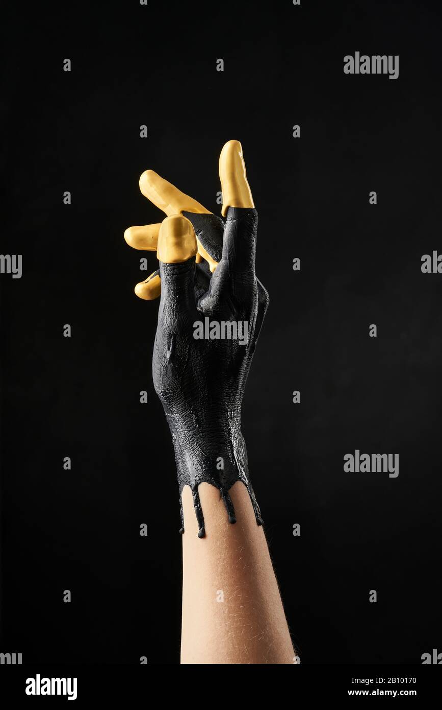 Female refined hand smeared with black and gold acrylic paint on a ...