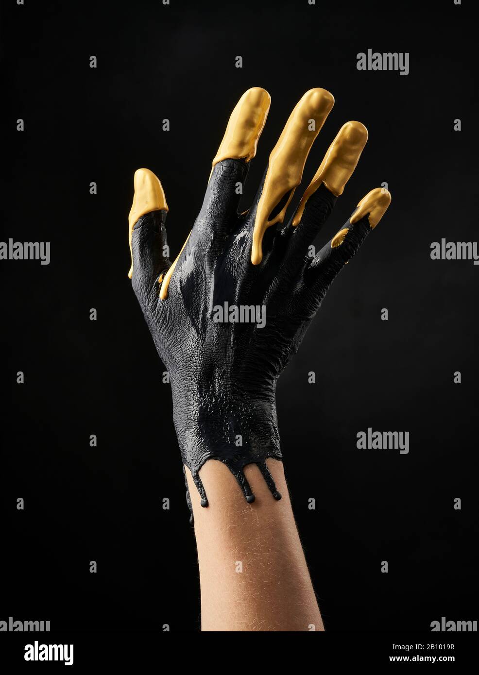 Female refined hand smeared with black and gold acrylic paint on a ...
