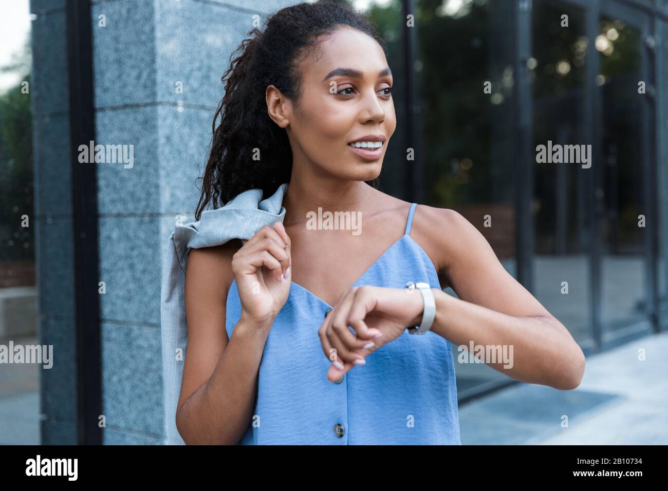 Attractive smiling african business woman standing outdoors at the city ...
