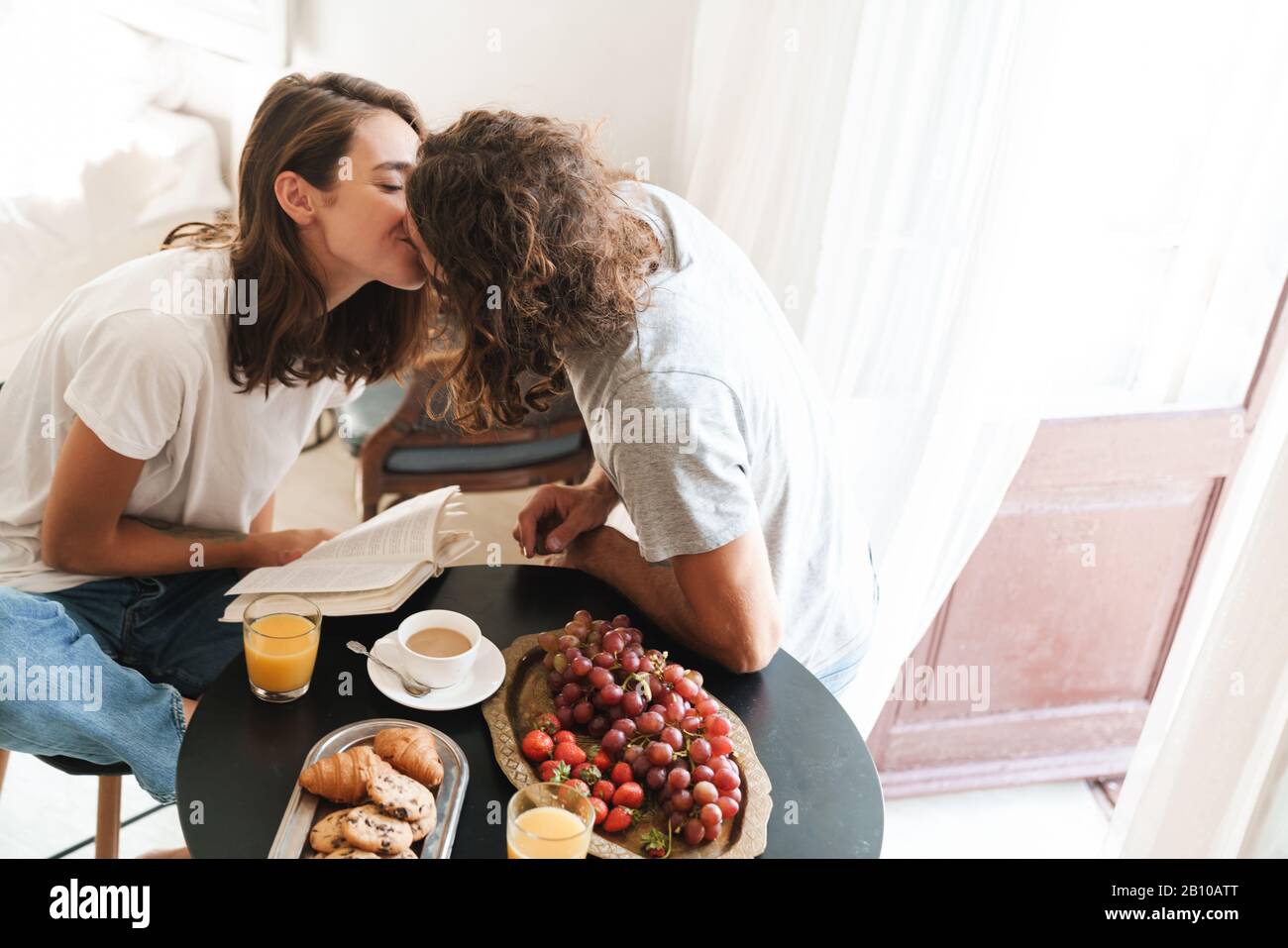 Picture of kissing cute loving couple indoors at home sit in kitchen at ...