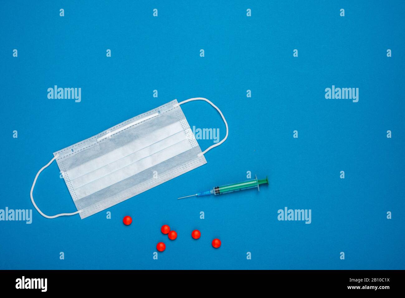 Red pills, green syringe and surgical mask with rubber ear straps ...