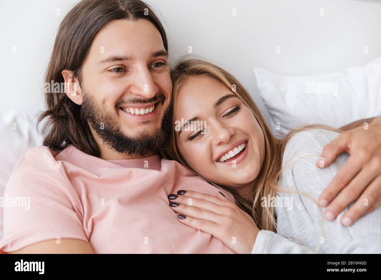 Beautiful smiling young couple laying in bed at home, embracing Stock ...