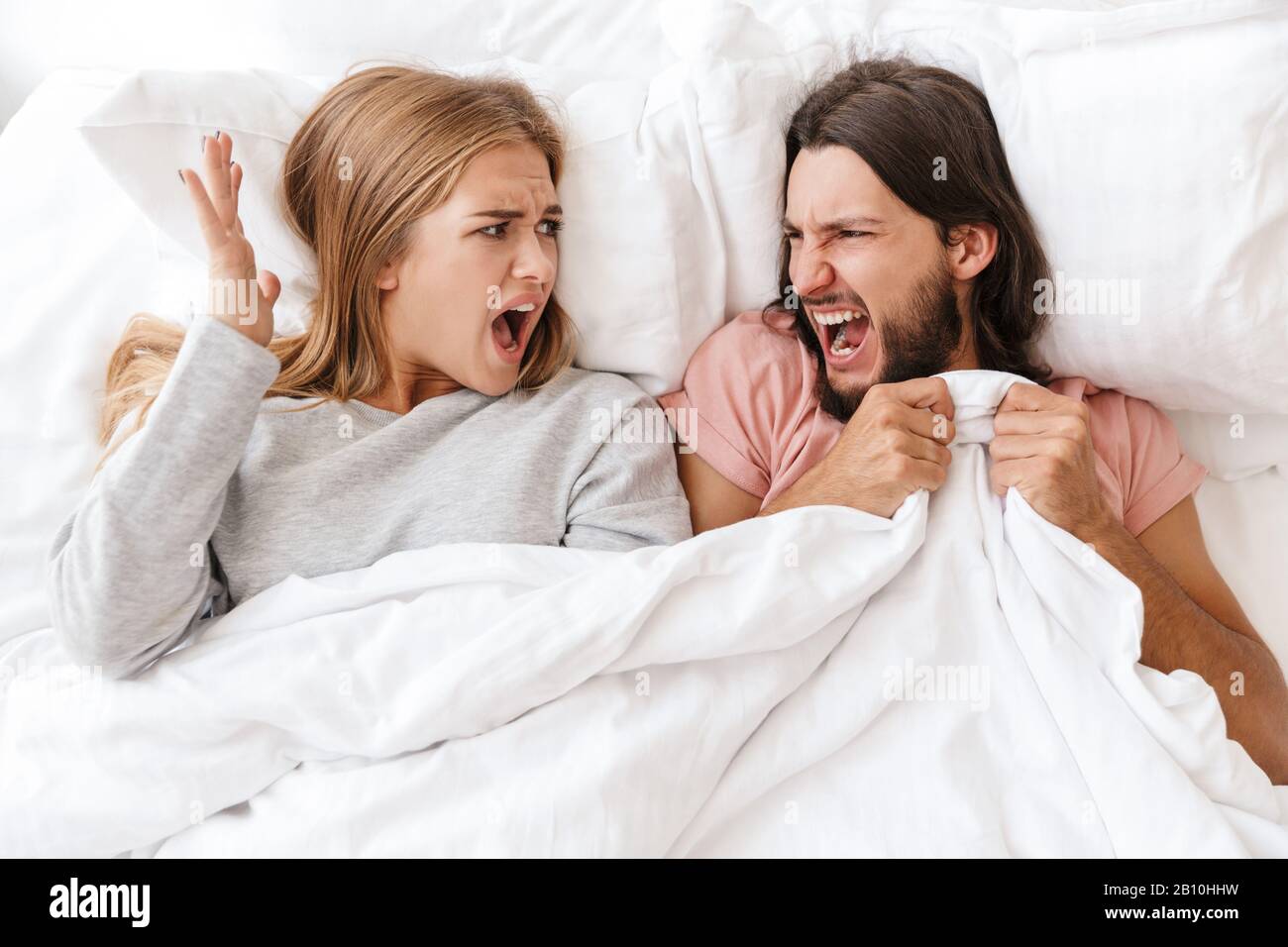 Beautiful angry young couple laying in bed at home, having a big ...