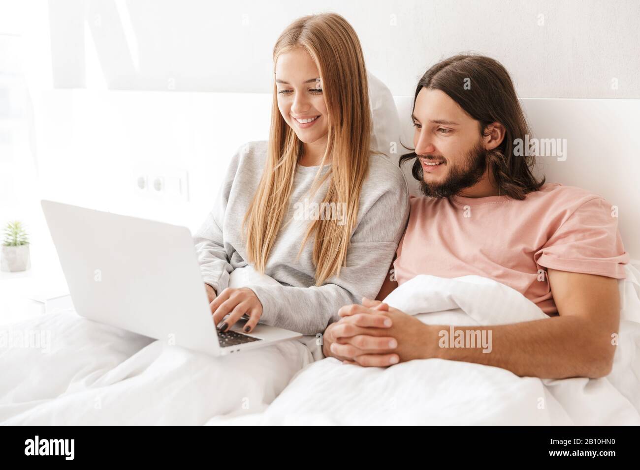 Photo of optimistic happy young loving couple in bed using laptop ...