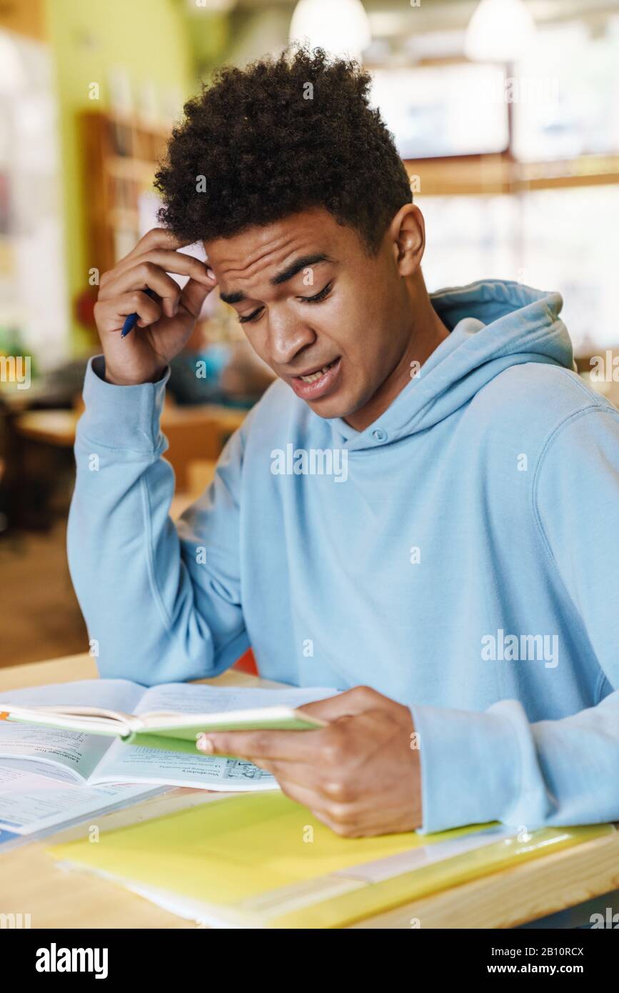 Serious african boy teenager studying while sitting at the hub indoors ...