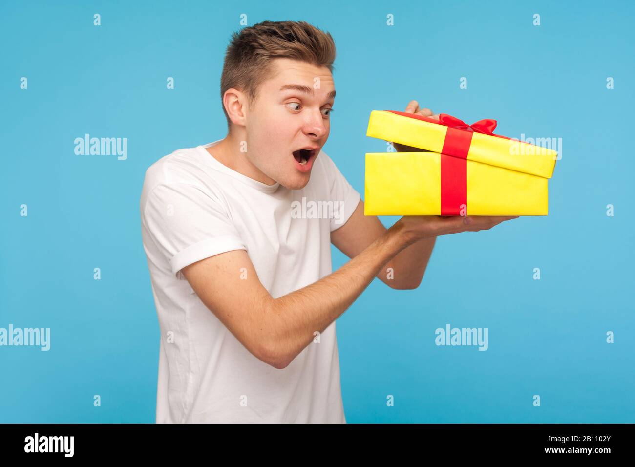 Shocked man in white t-shirt looking inside gift box with curious and ...