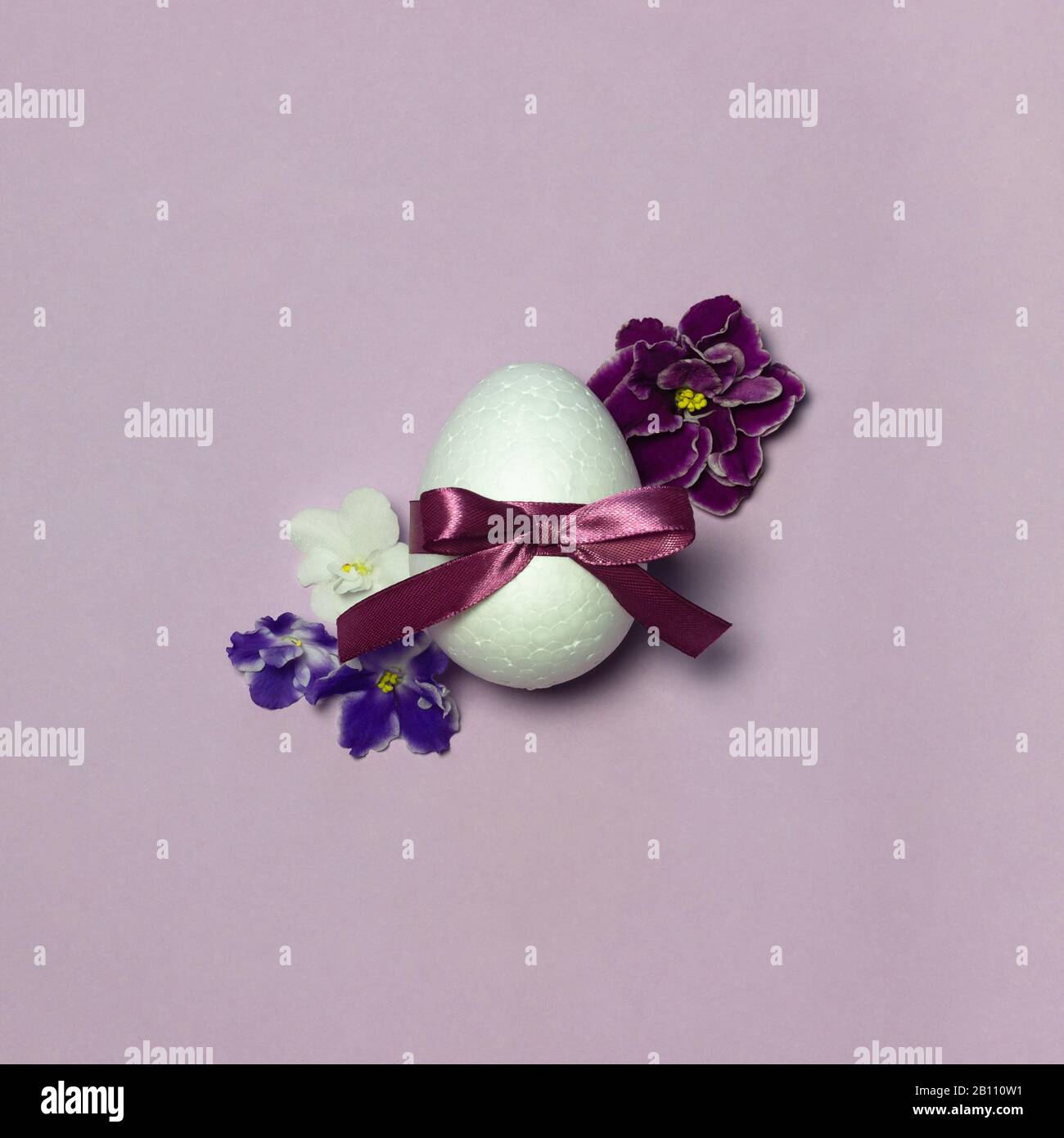 White egg with ribbon and violets on purple background. Happy Easter ...