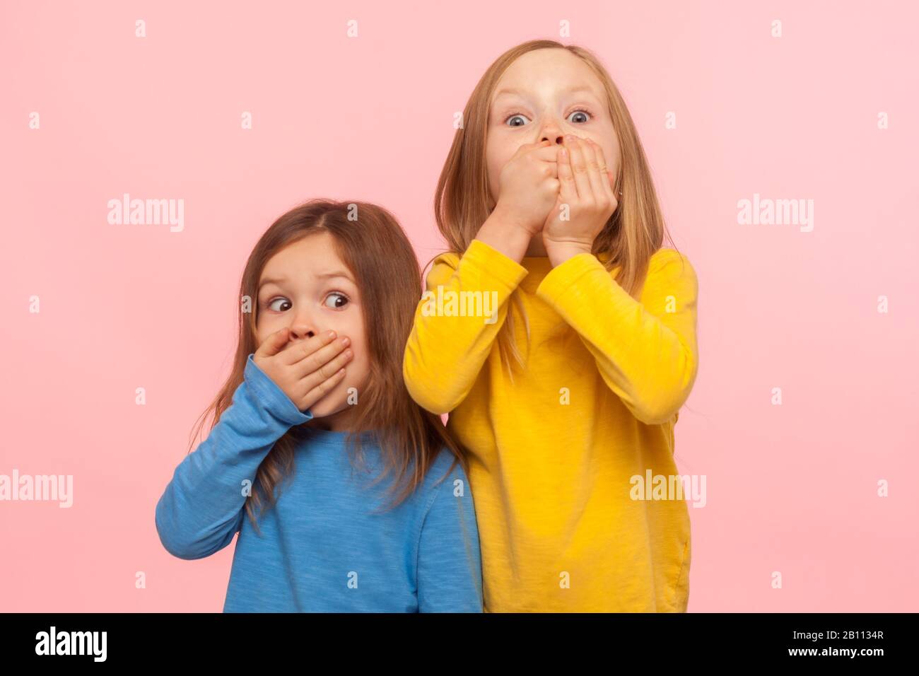 Portrait of two little frightened girls covering mouth with hands and ...