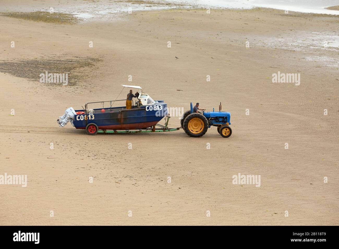 Blue tractor with yellow wheels towing trailer with fishing boat across ...