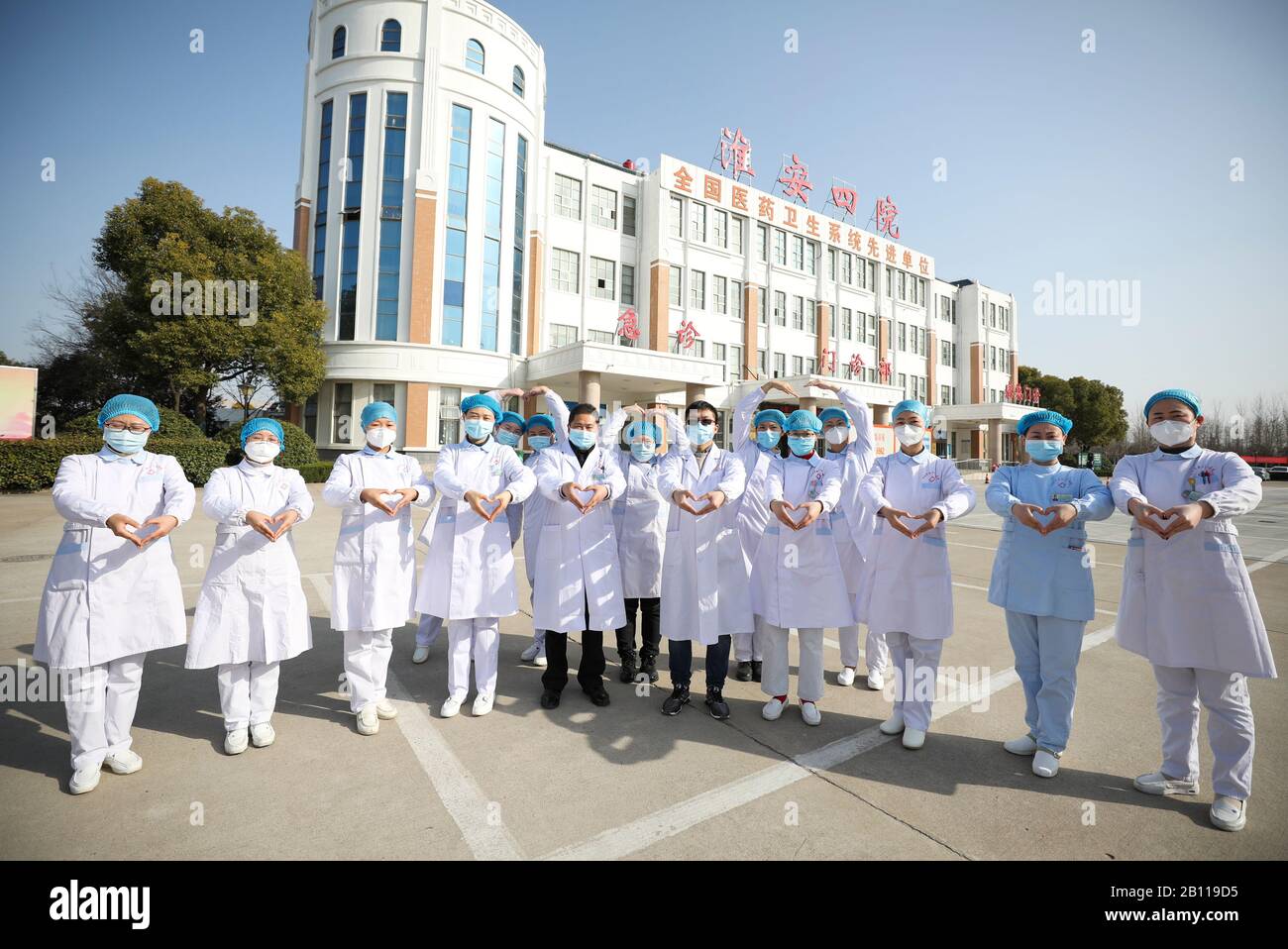 Masked Chinese medical workers make hearts with their hands as they go ...