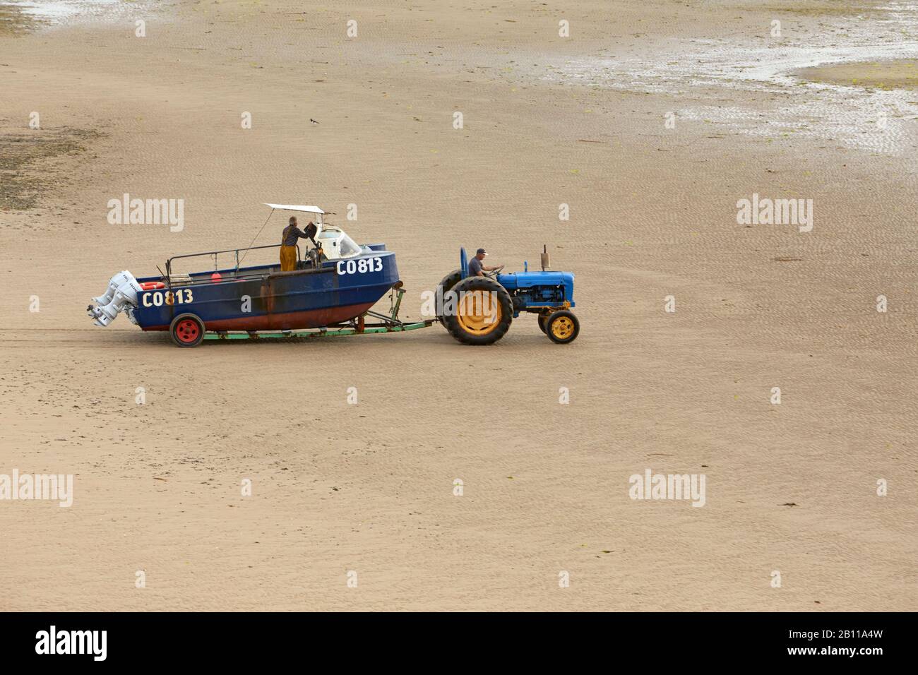 Blue tractor with yellow wheels, towing fishing boat on trailer across ...