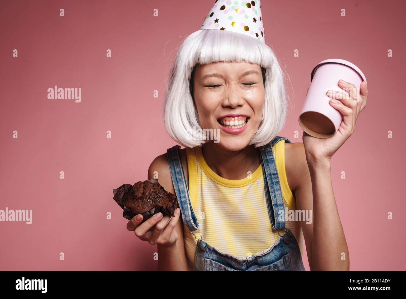 Image of young asian girl wearing party cone drinking coffee and eating ...