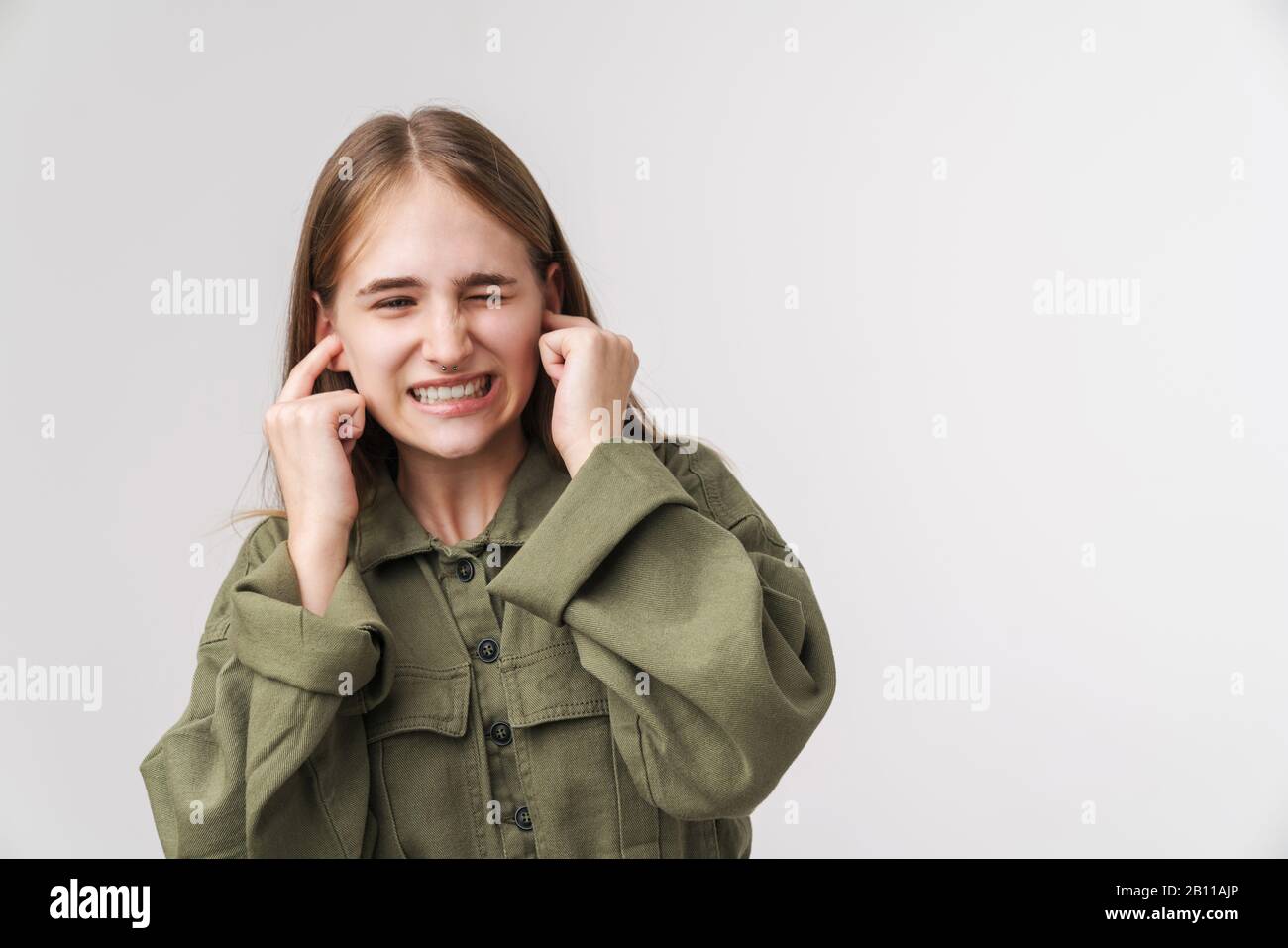 Photo of irritated young woman plugging her ears and looking aside ...