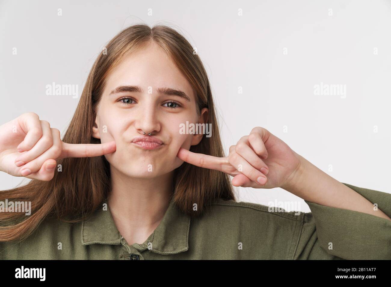 Photo of funny caucasian woman pointing fingers at cheeks and grimacing ...