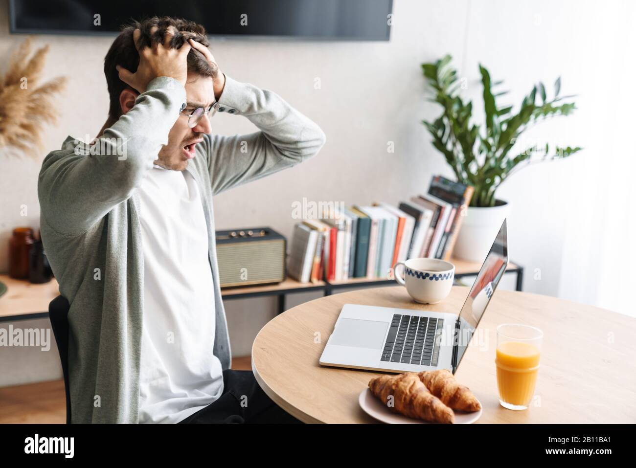 Image of disappointed young man in eyeglasses grabbing his head and ...