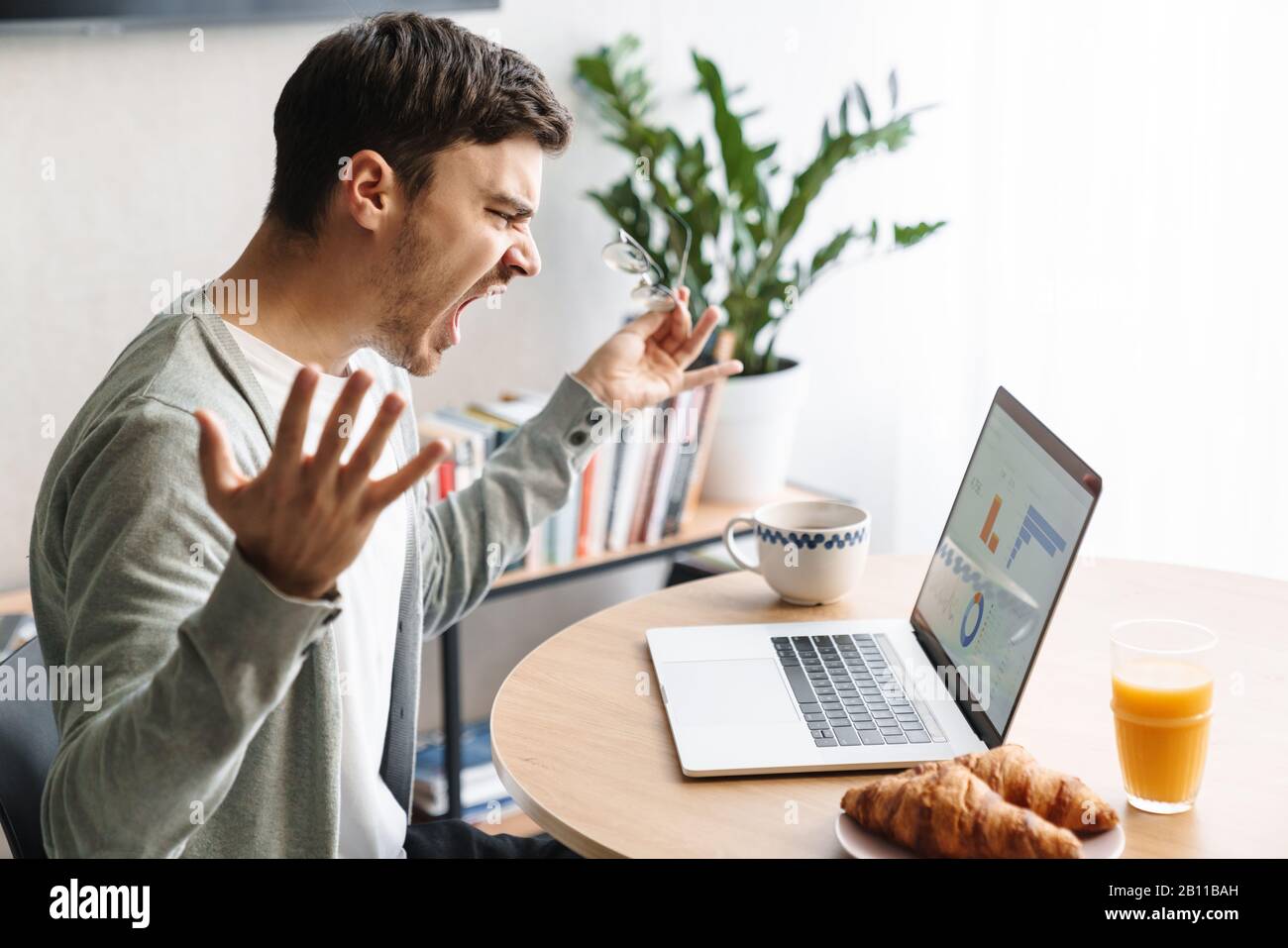 Image of angry young man in eyeglasses screaming and looking at screen ...