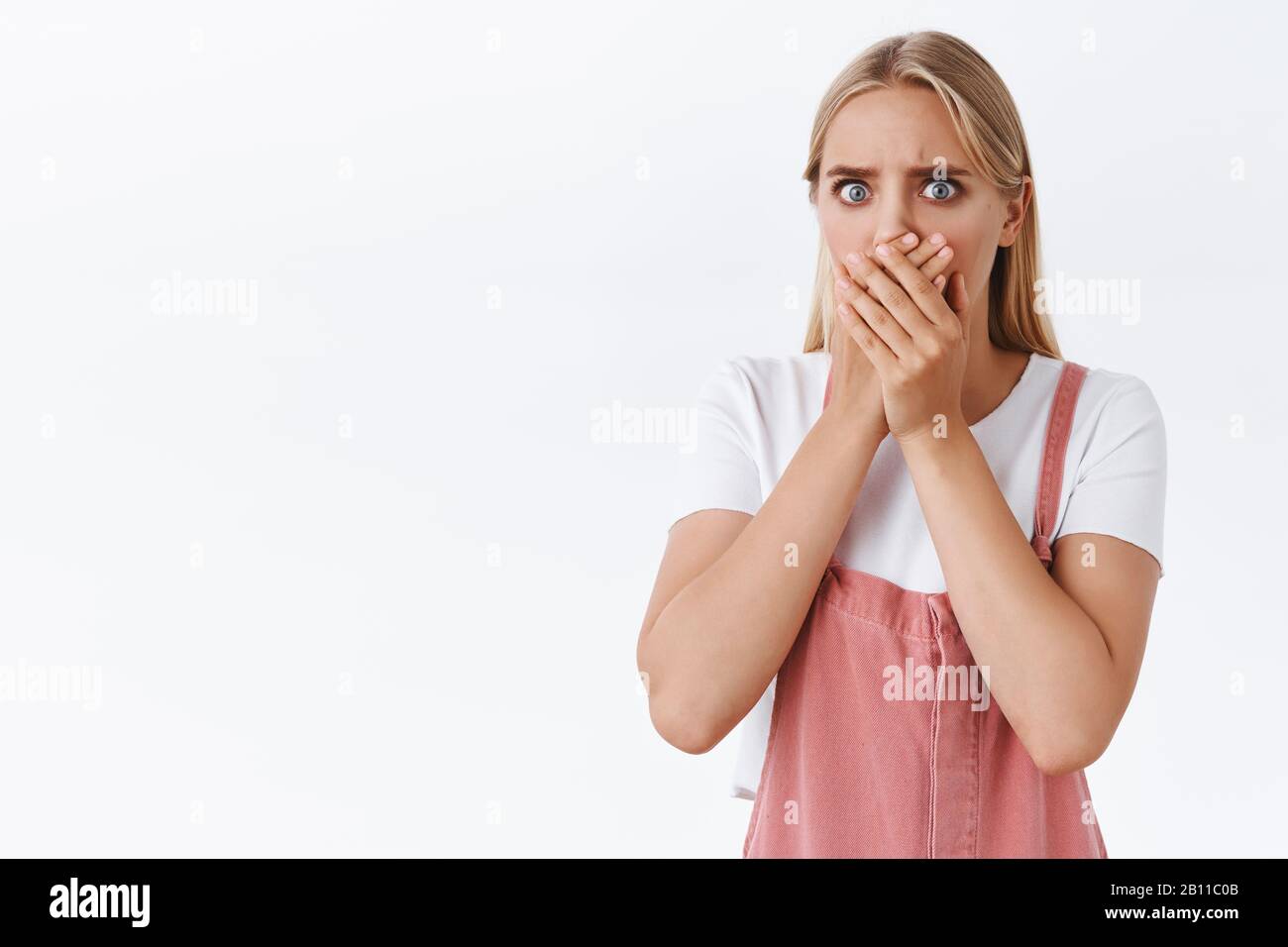 Shocked and disgusted young uneasy blond girl in pink overalls, t-shirt ...