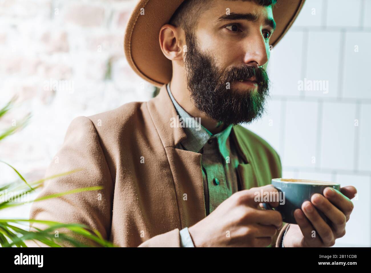 Image of attractive stylish young man wearing hat drinking tea from cup ...