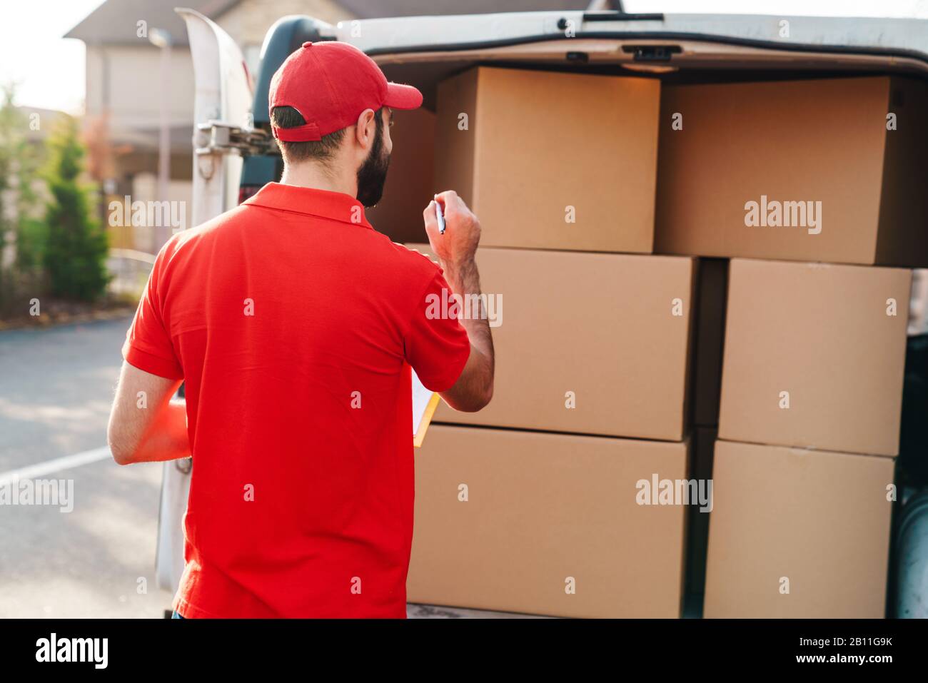 Image of young delivery man in red uniform holding clipboard and ...