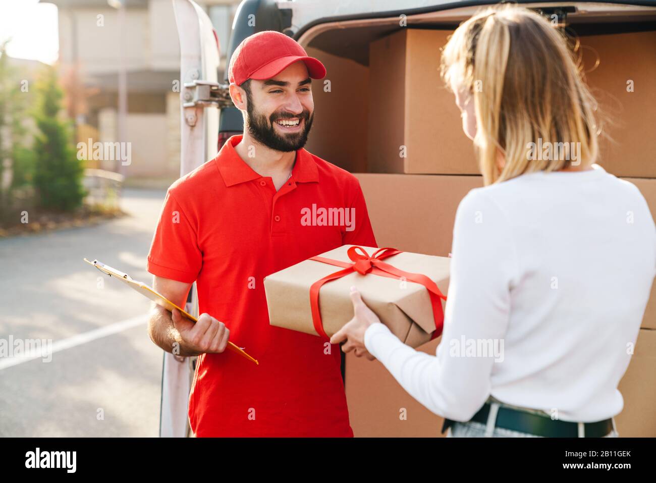 Image of cheerful delivery man in red uniform getting order from ...