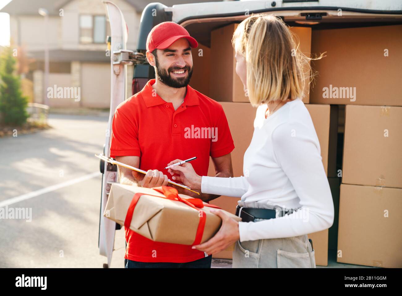 Image of cheerful delivery man in red uniform getting order from ...