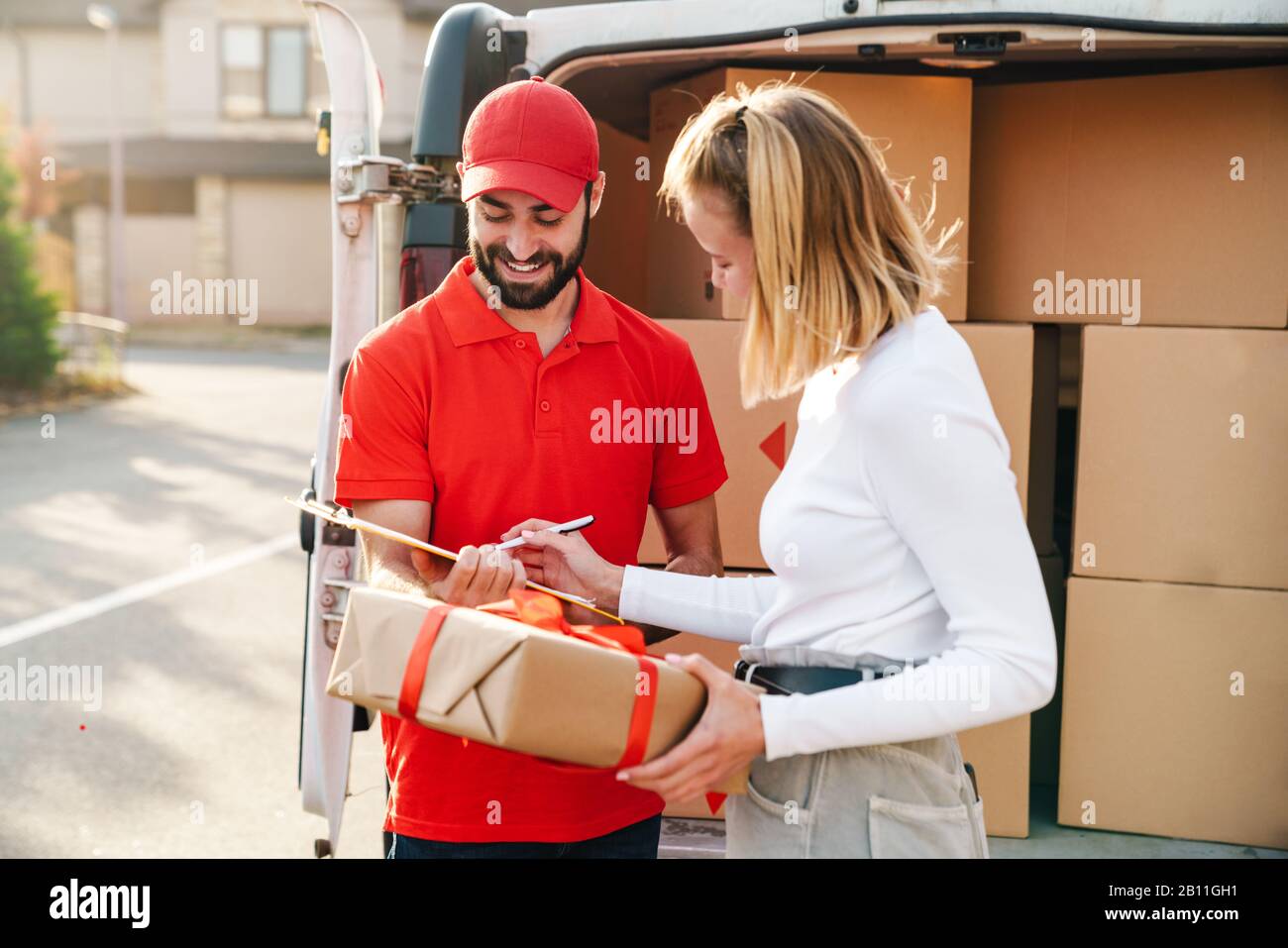 Image of cheerful delivery man in red uniform getting order from ...