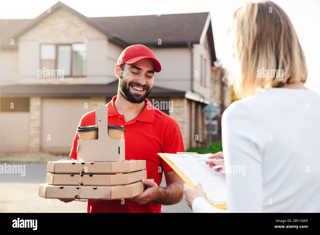 Image of smiling delivery man in red uniform giving food order to ...