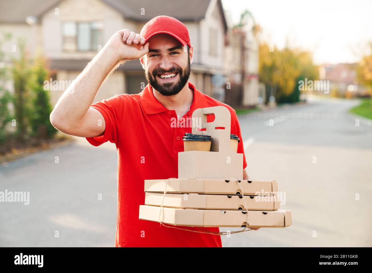 Image of joyful young delivery man in red uniform holding pizza boxes ...